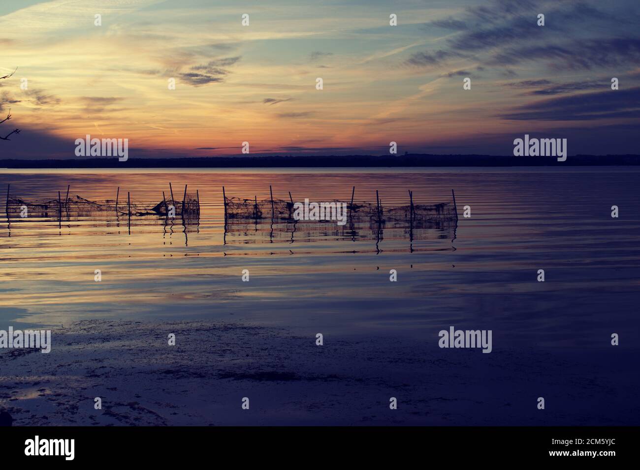 Sunset over water, Belmont Bay with netting fence in shallow water in ...