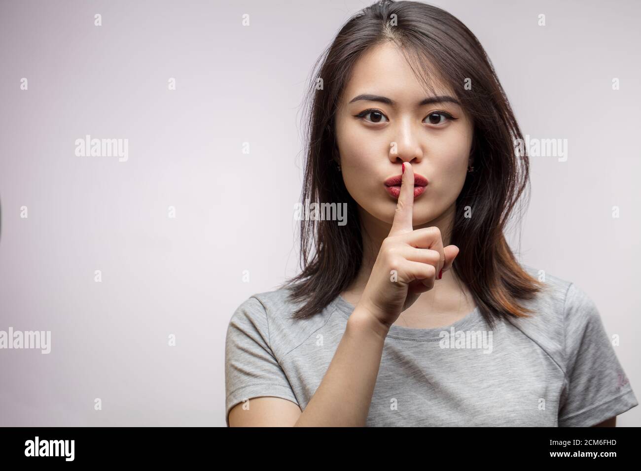Asian female model keeping index finger near mouth making hush sign ...