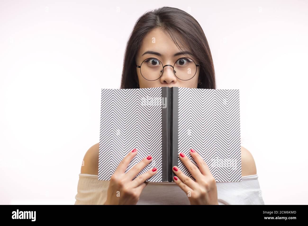 Asian student female wearing spectacles covers her face with grey book ...