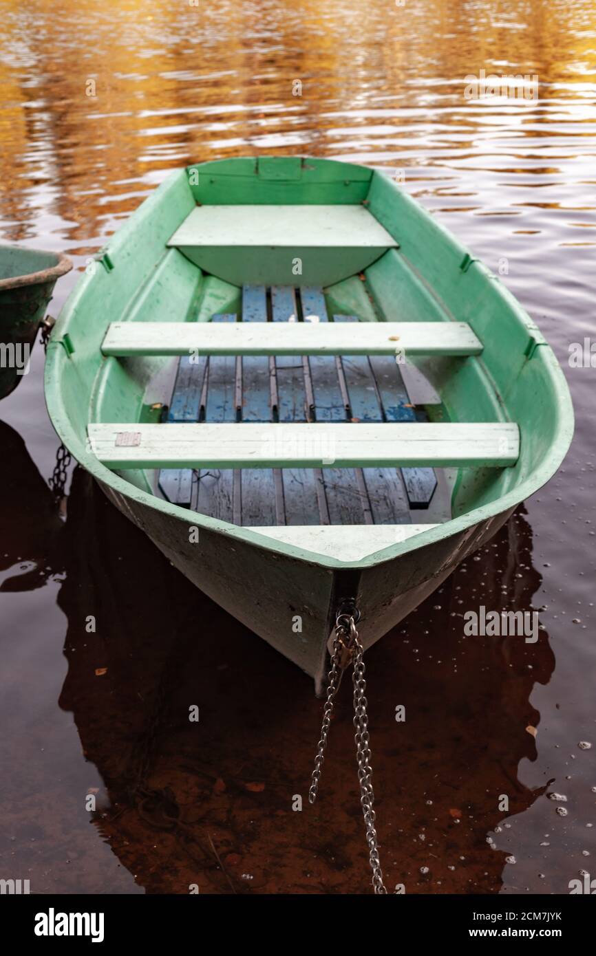Small green rowboat is moored at coast of a still lake, vertical photo ...