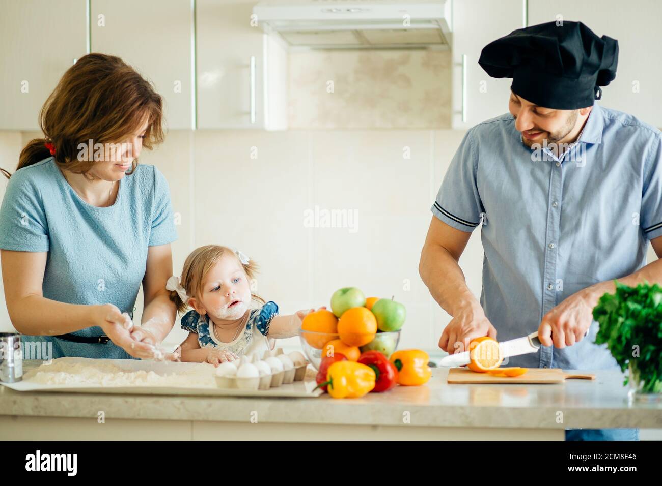 Happy young family with Mum, Dad and two young children cooking in the ...