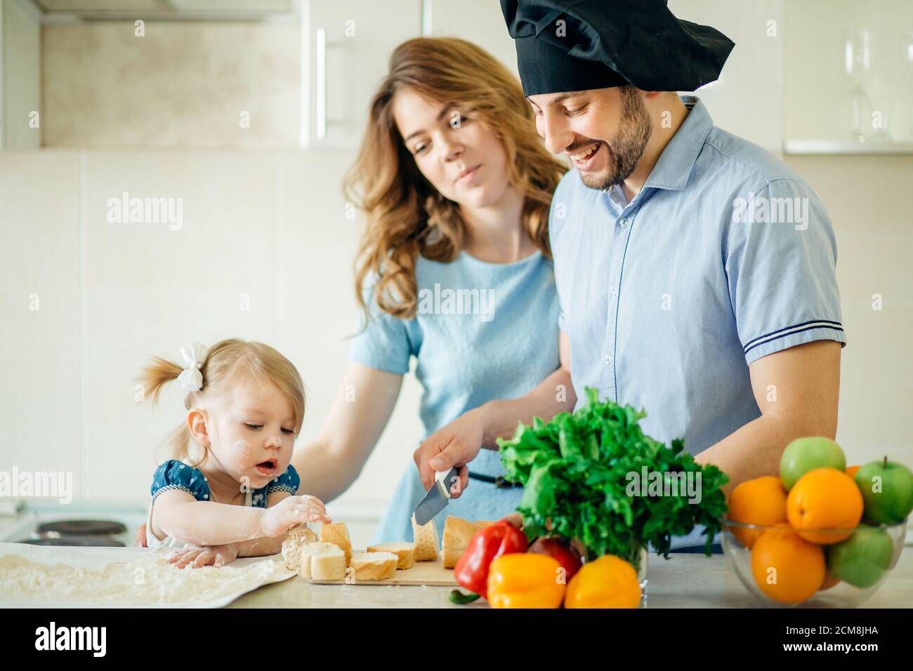 Happy young family with Mum, Dad and two young children cooking in the ...