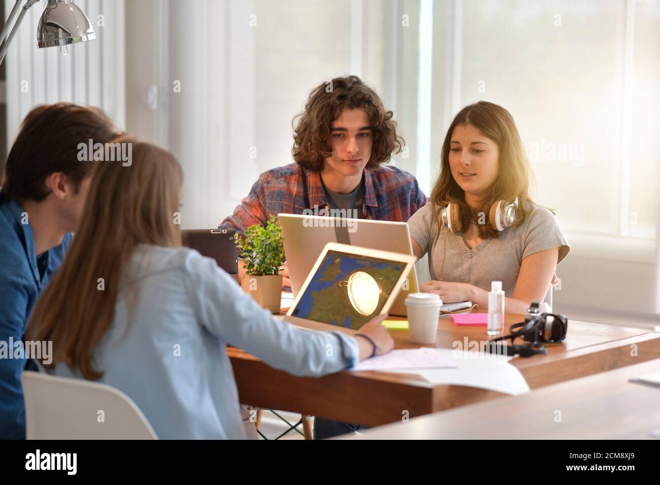 Young students meeting aroud table to work on project Stock Photo - Alamy