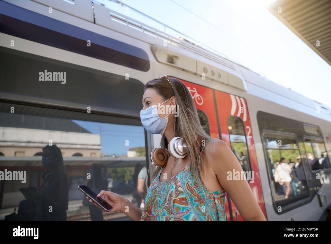 Young woman waiting for train on railway platform, wearing face mask ...