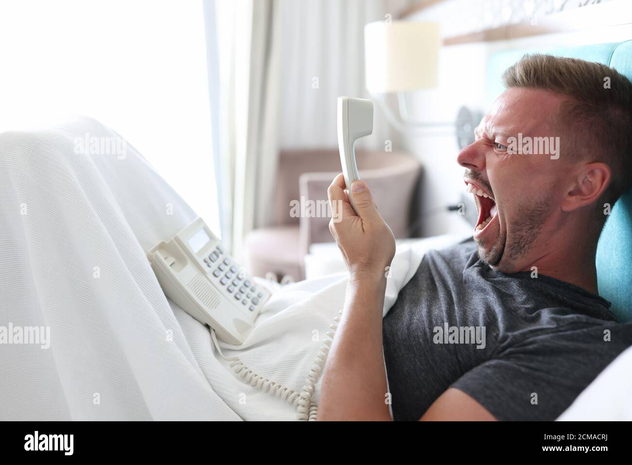 Angry man lies in bed and shout into white phone receiver Stock Photo ...