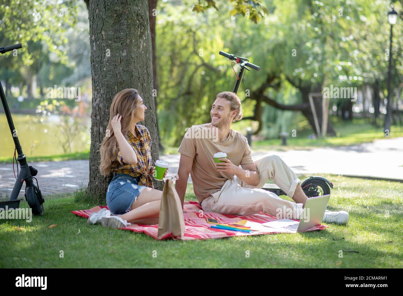 Two young people sitting under the tree and talking Stock Photo - Alamy
