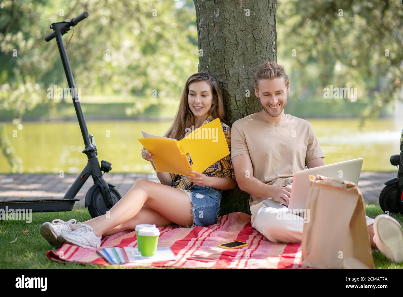 Two young people sitting under the tree and studying together Stock ...