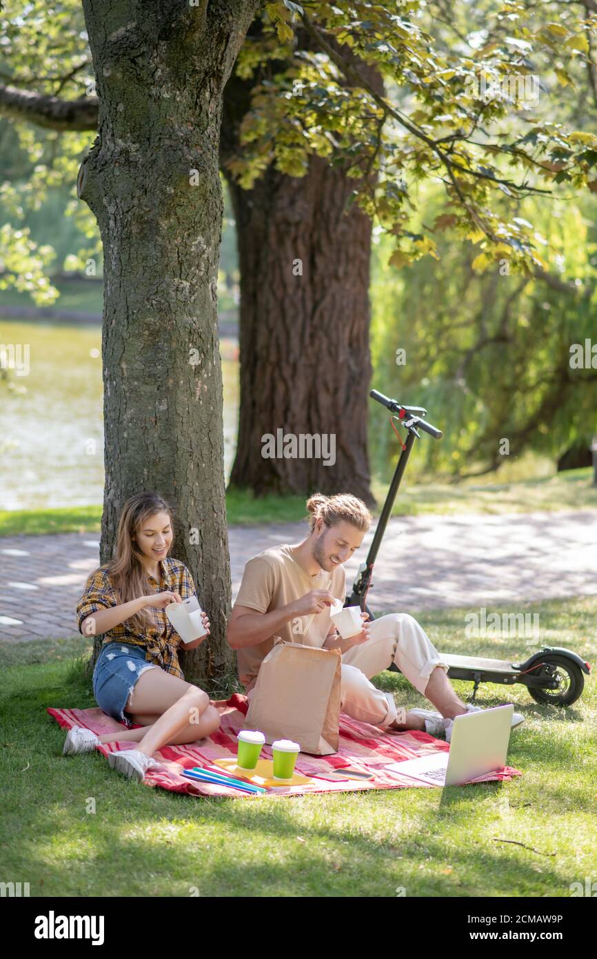Young couple sitting under the tree and eating Stock Photo - Alamy