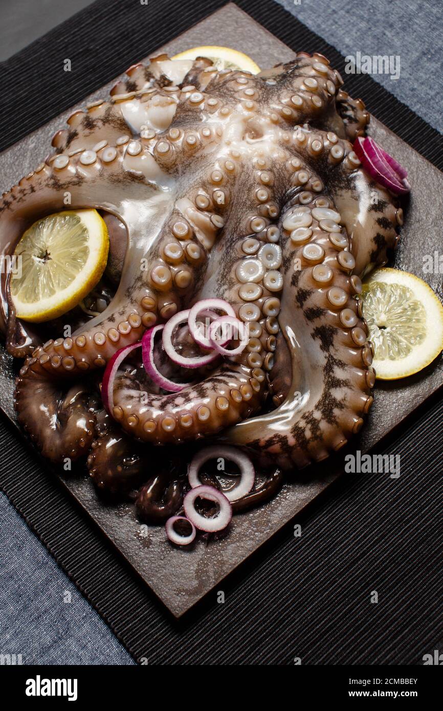 Seafood, whole raw big octopus on a stone dish served with lemon and ...