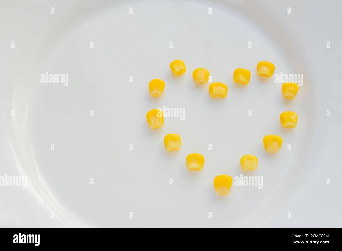 Close up of sweet corn in shape of heart on white plate. Copy space for ...