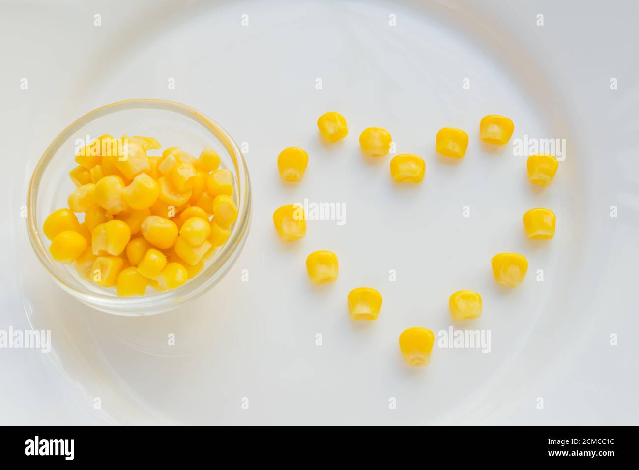 Close up of sweet corn in shape of heart on white plate. Bowl with ...