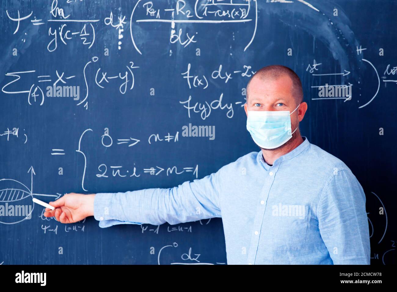 Male teacher with mask teaching math lesson at school. Social ... Male teacher with mask teaching math lesson at school. Social ...