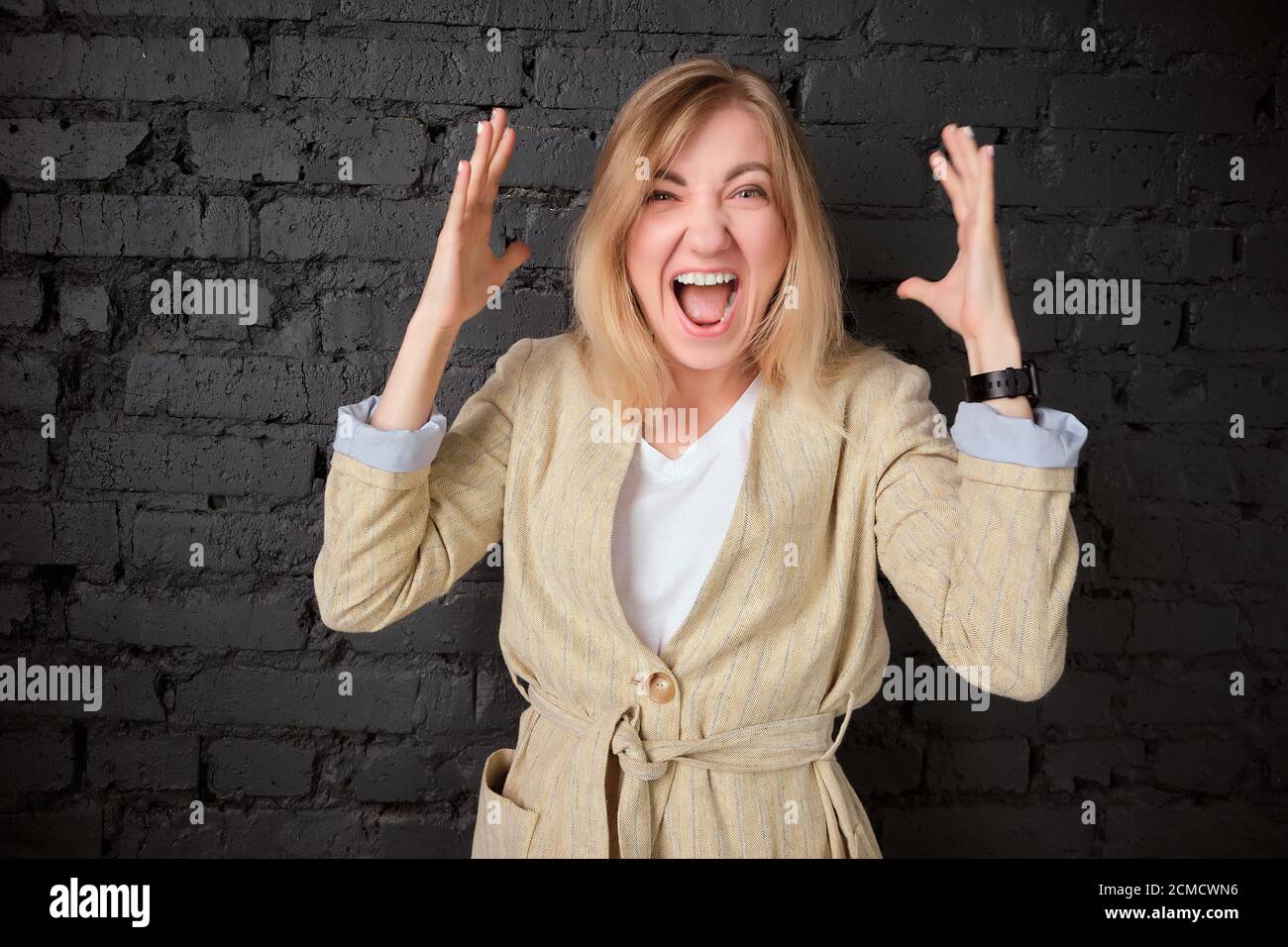 Young woman screaming opposite black brick wall. Emotional portrait of ...