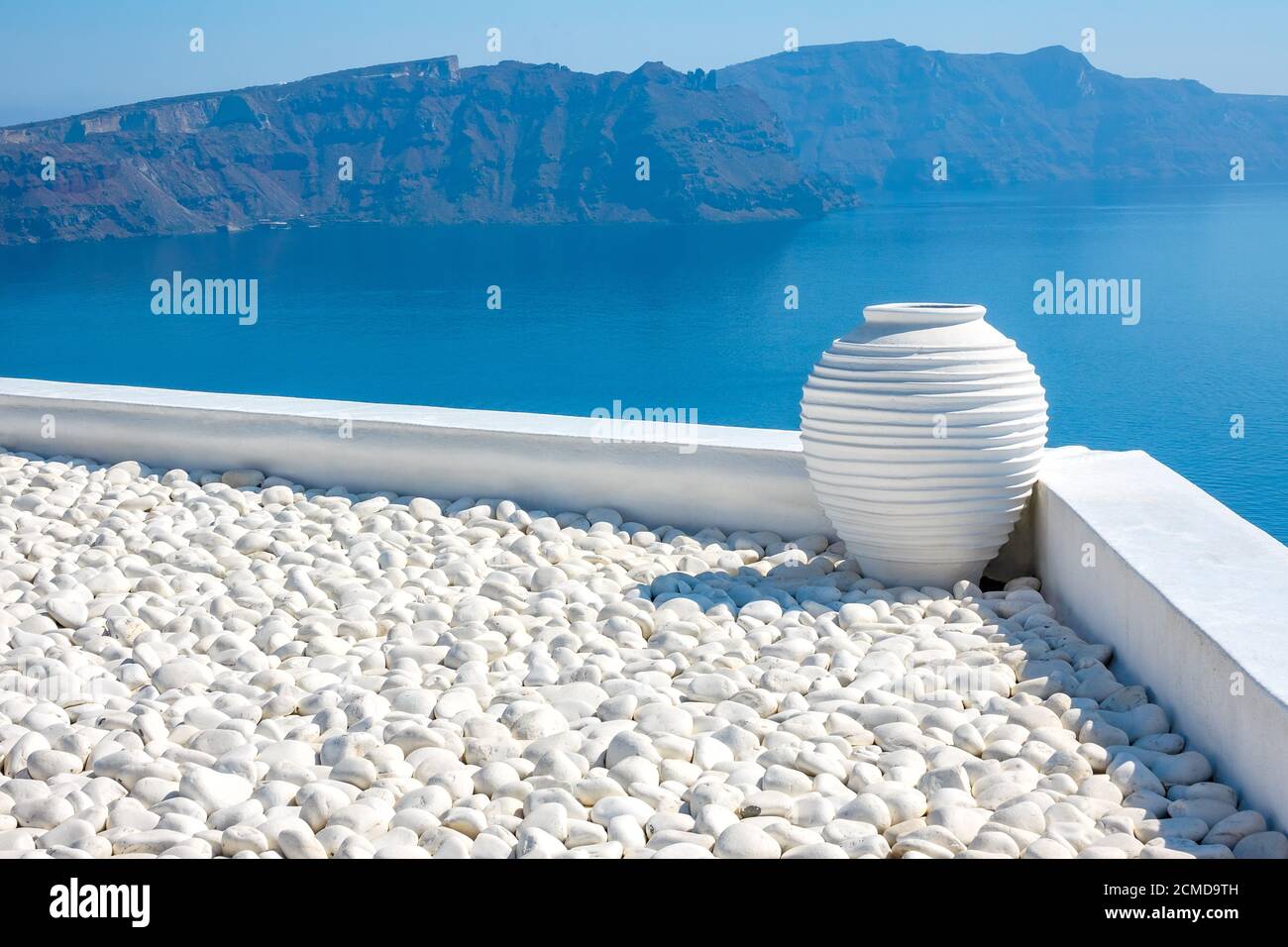 Greece. Sunny day on Santorini. White pebbles and white stone vase ...