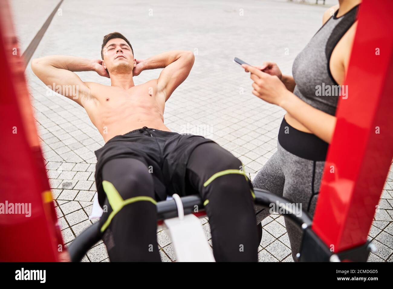 Muscular man training abdominal with girlfriend support outdoors Stock ...