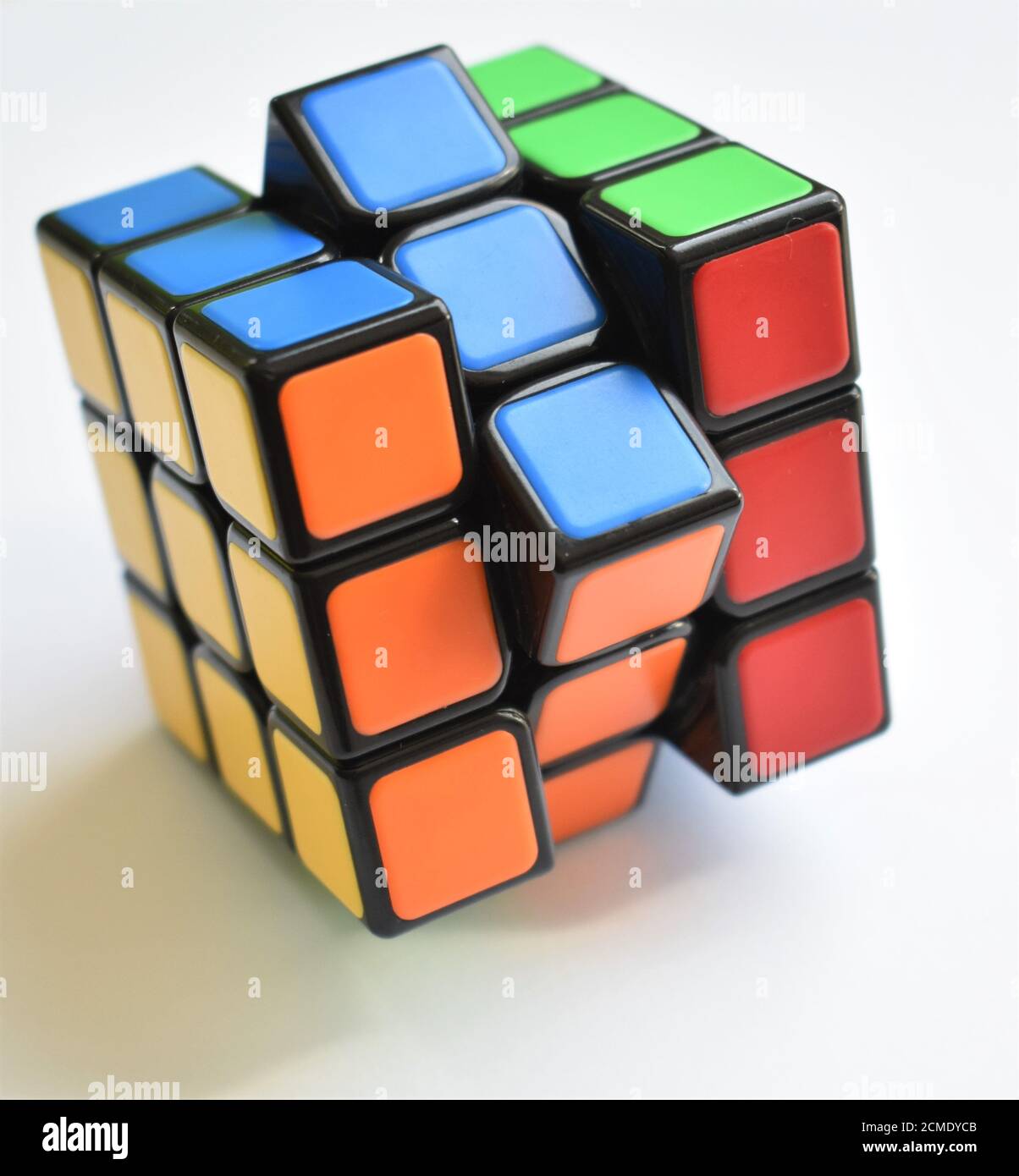 An isolated Rubik's Cube puzzle sits almost solved on a crisp white background in bright natural ...