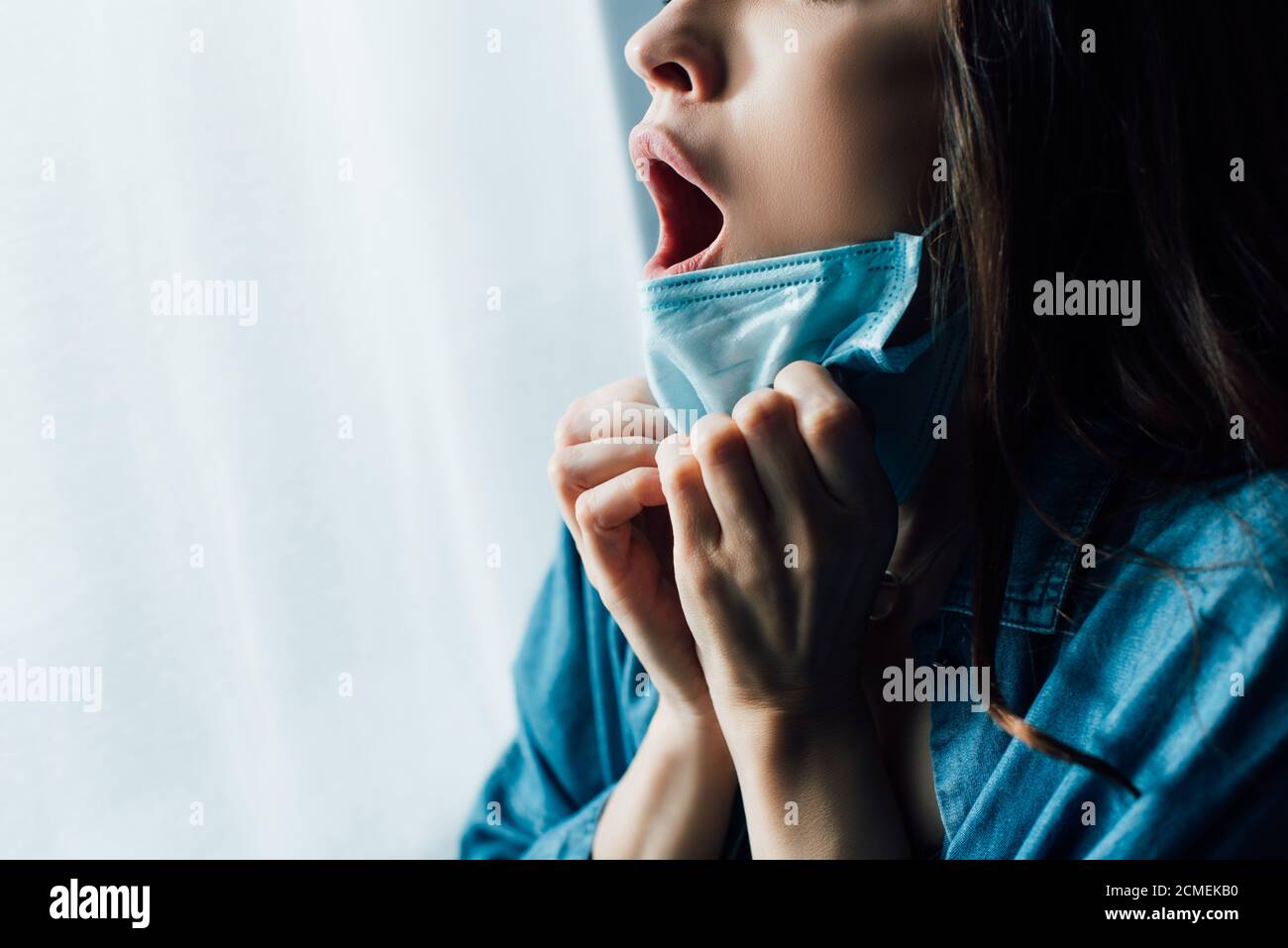 partial view of scared woman with open mouth touching medical mask ...