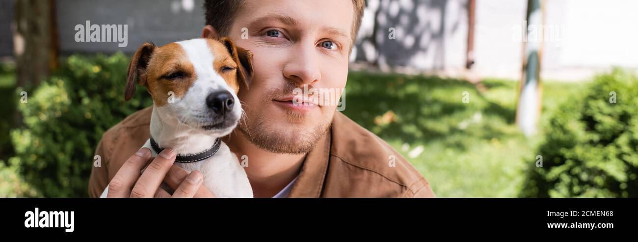 panoramic shot of man cuddling jack russell terrier dog while looking ...