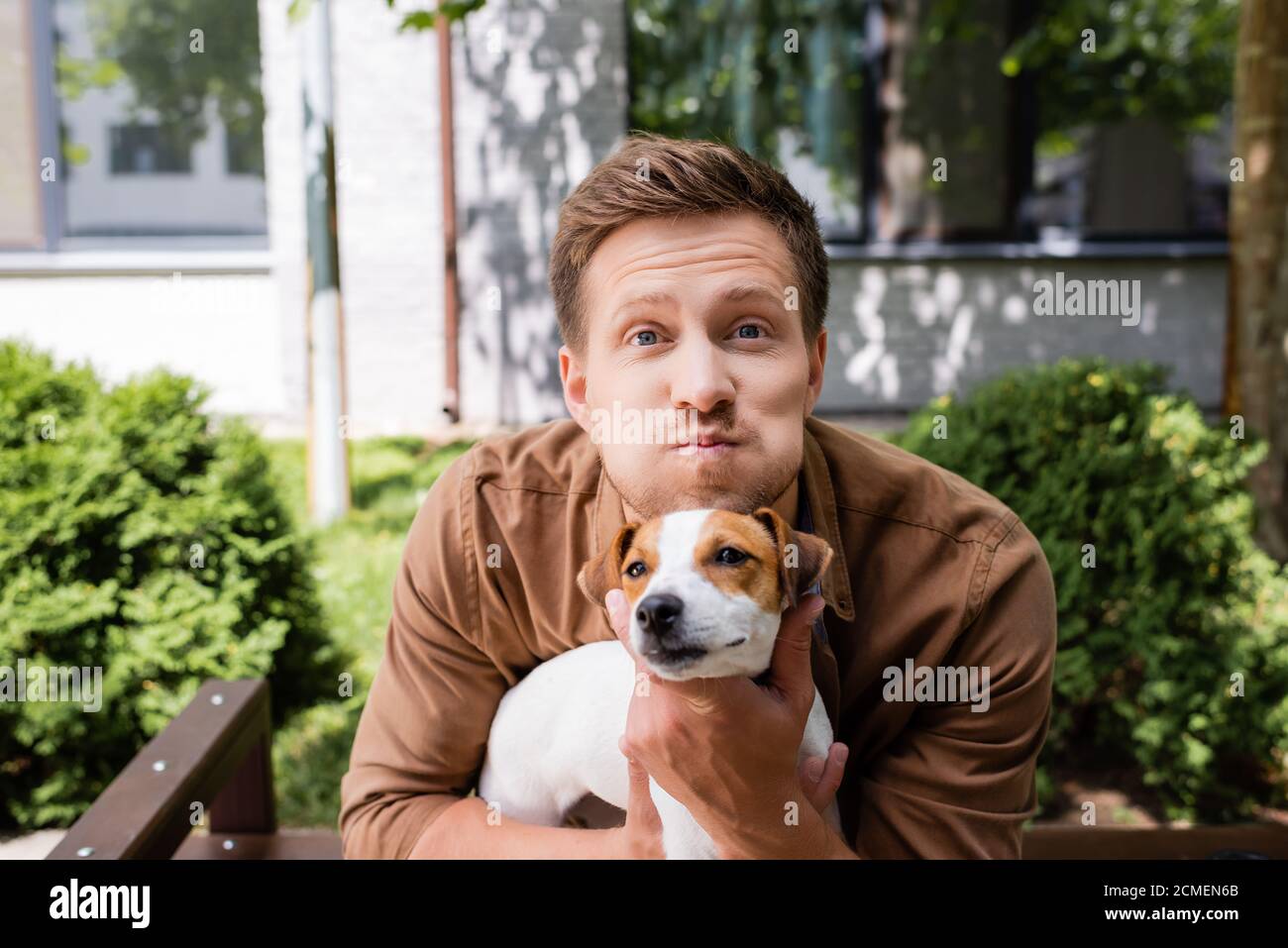 young man grimacing and puffing out cheeks while holding jack russell ...