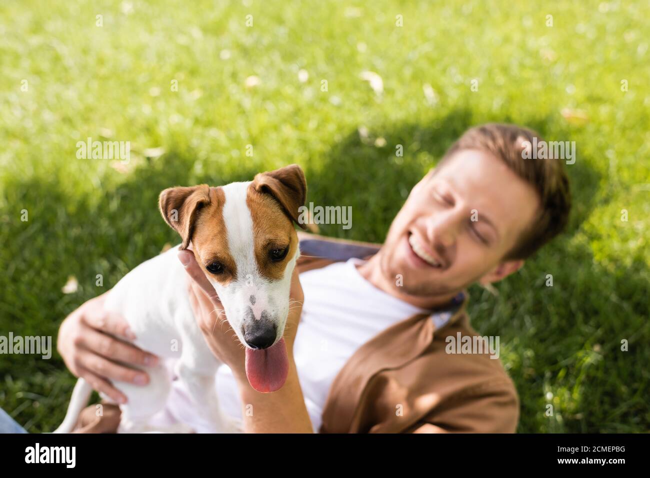 young man holding jack russell terrier dog while relaxing on green ...