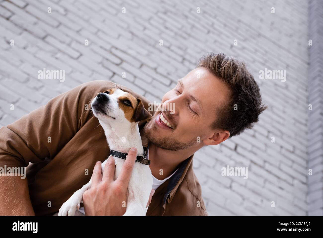 Low angle view of young man embracing jack russell terrier near ...