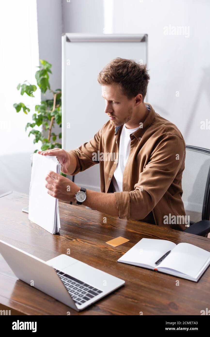 Selective focus of businessman holding papers near notebook and laptop ...