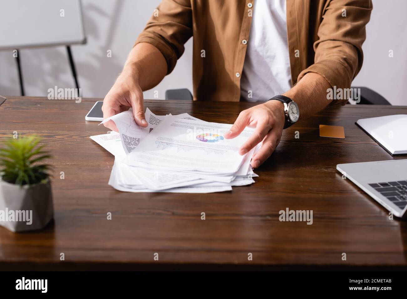 Cropped view of businessman taking documents near gadgets on table in ...