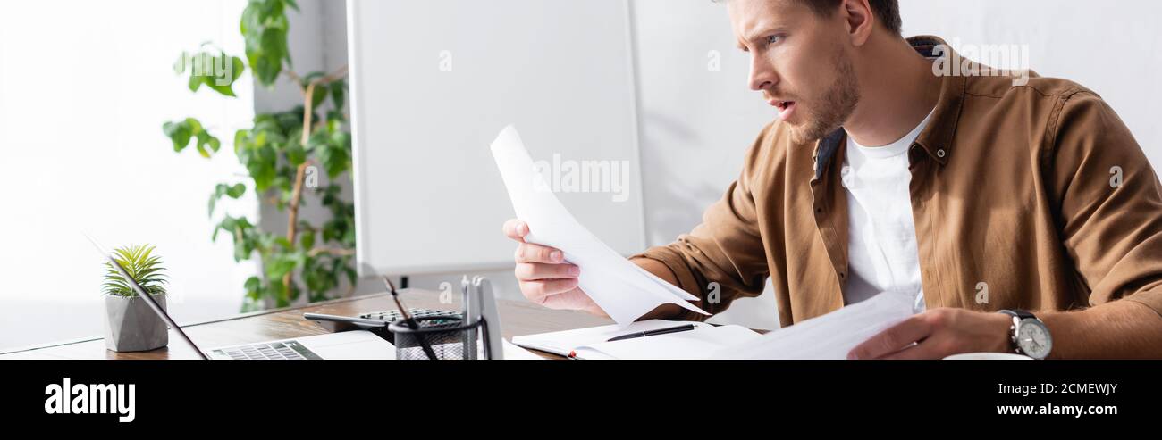 Horizontal crop of focused businessman looking at papers at table in ...