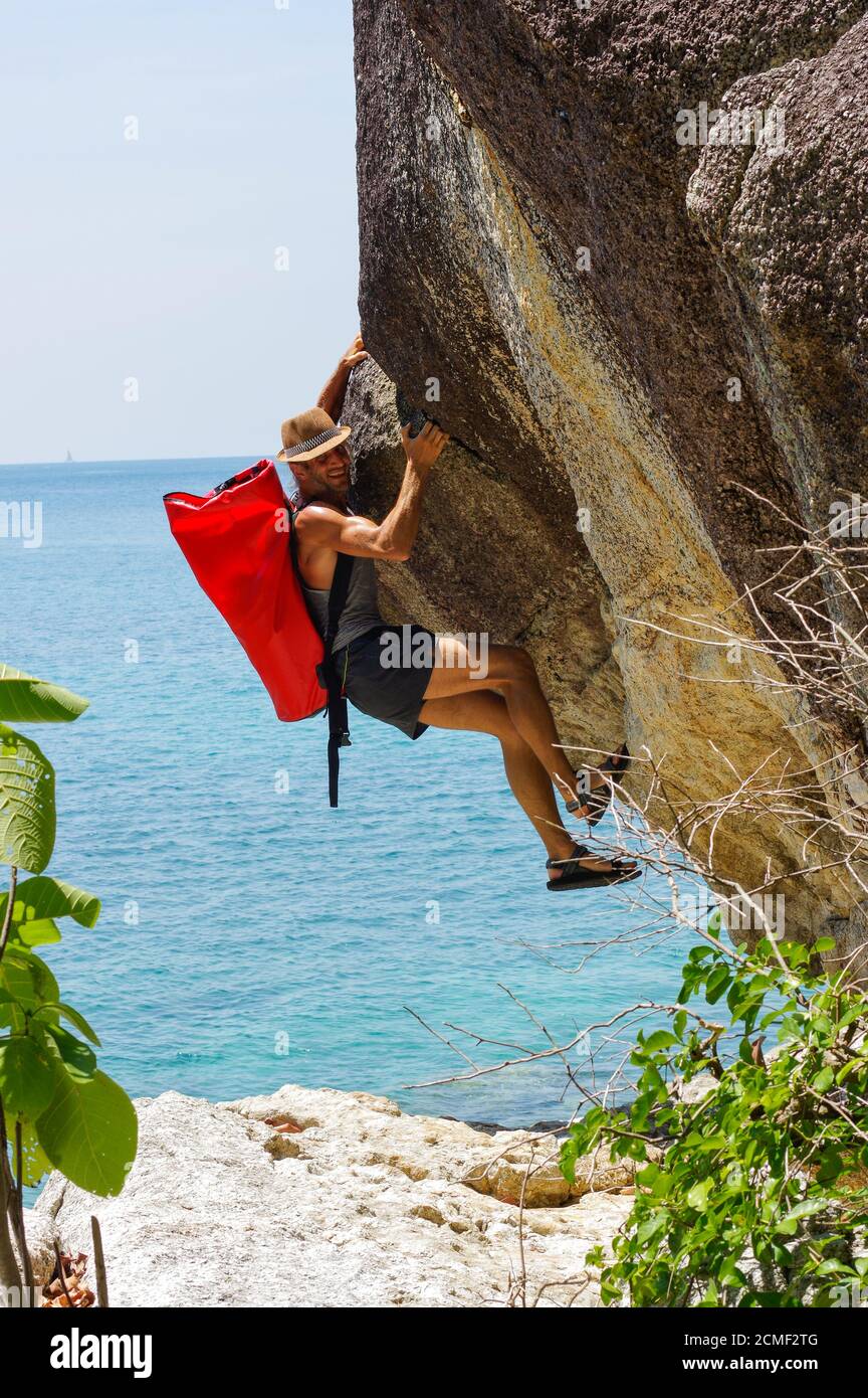 strong and happy man climbing on high rock over the sea with a hut red ...