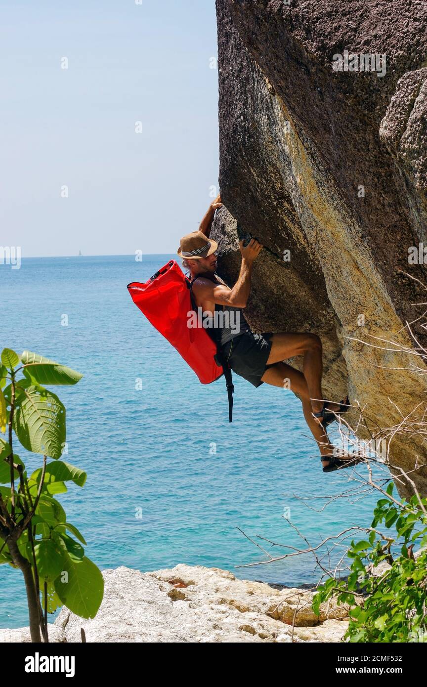 strong and happy man climbing on high rock over the sea with a hut red ...