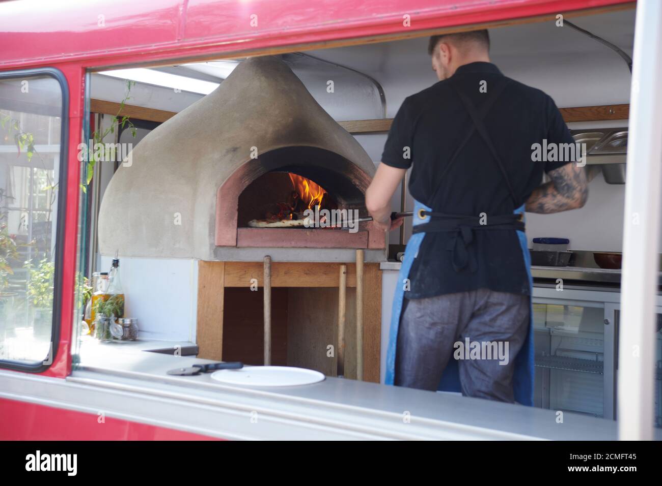 chef removing hot pizza from the wood-fired oven in a mobile pizza van ...