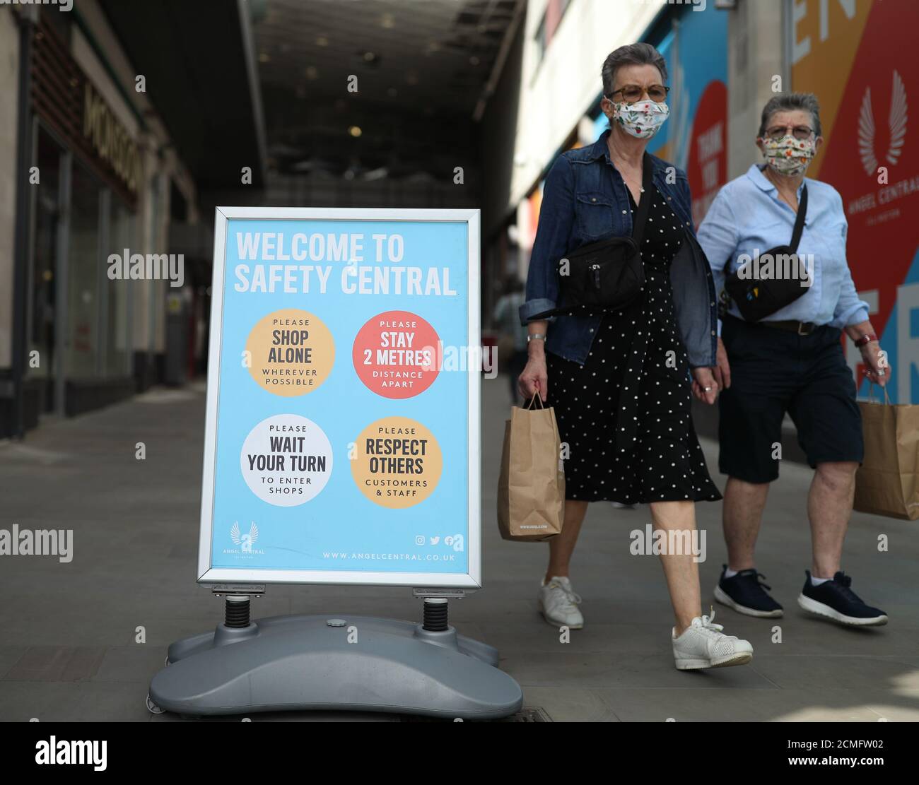 Shoppers walk past a social distancing information sign at a shopping ...