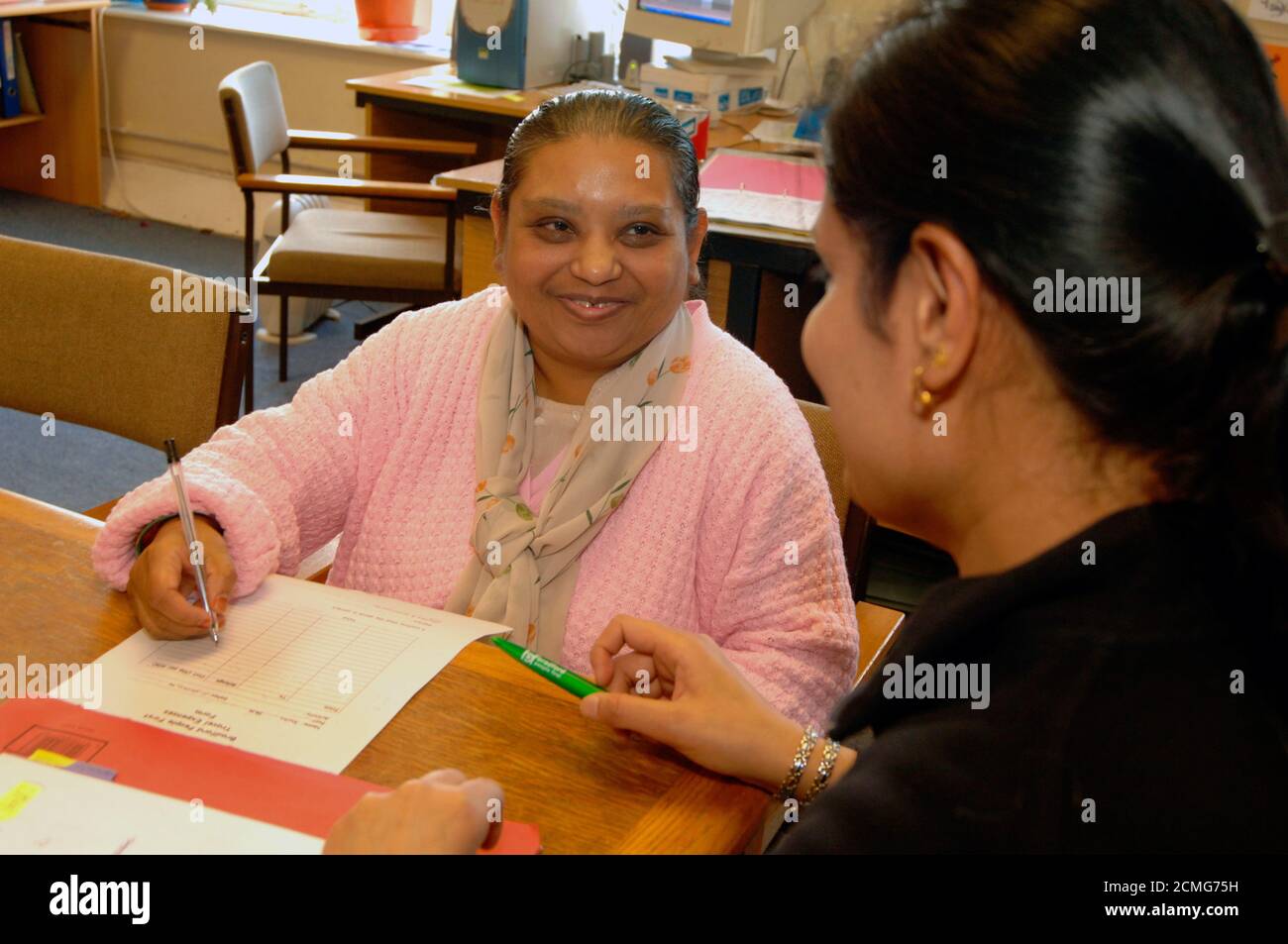 Woman with learning disabilities filling in form with carer at ...
