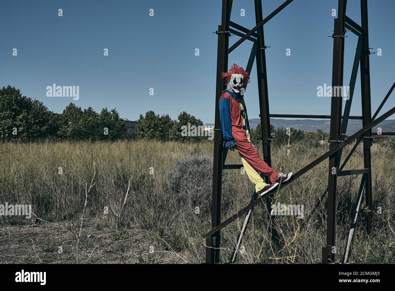 a scary evil clown, wearing a yellow, red and blue costume outdoors ...