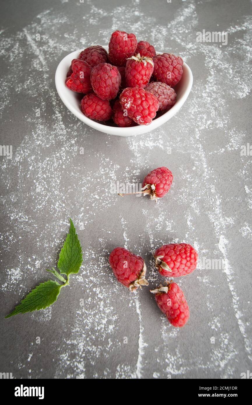 Ripe raspberries in a bowl on a gray stone table with scattered ...