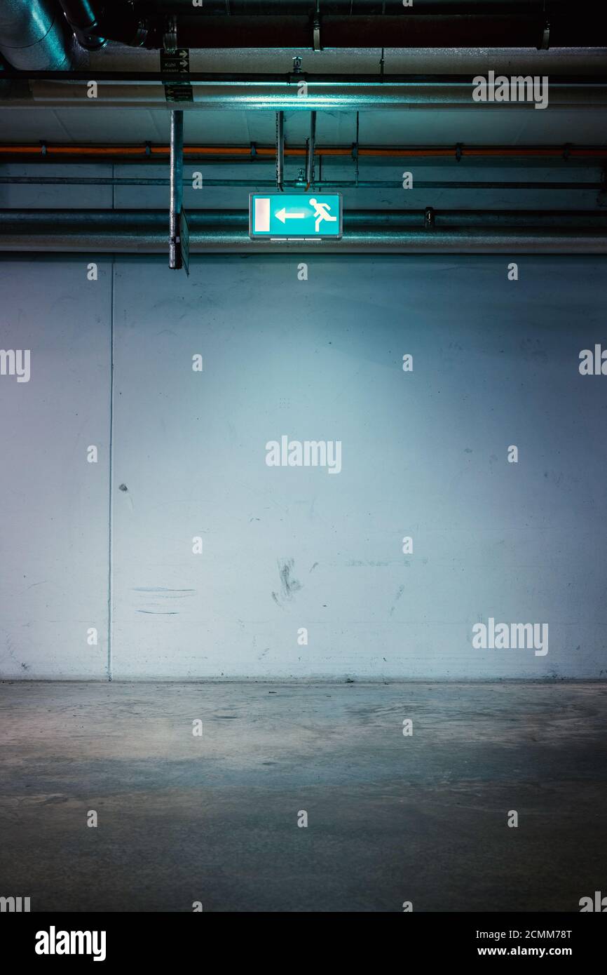 The green illuminated emergency exit notice hangs under the ceiling in ...
