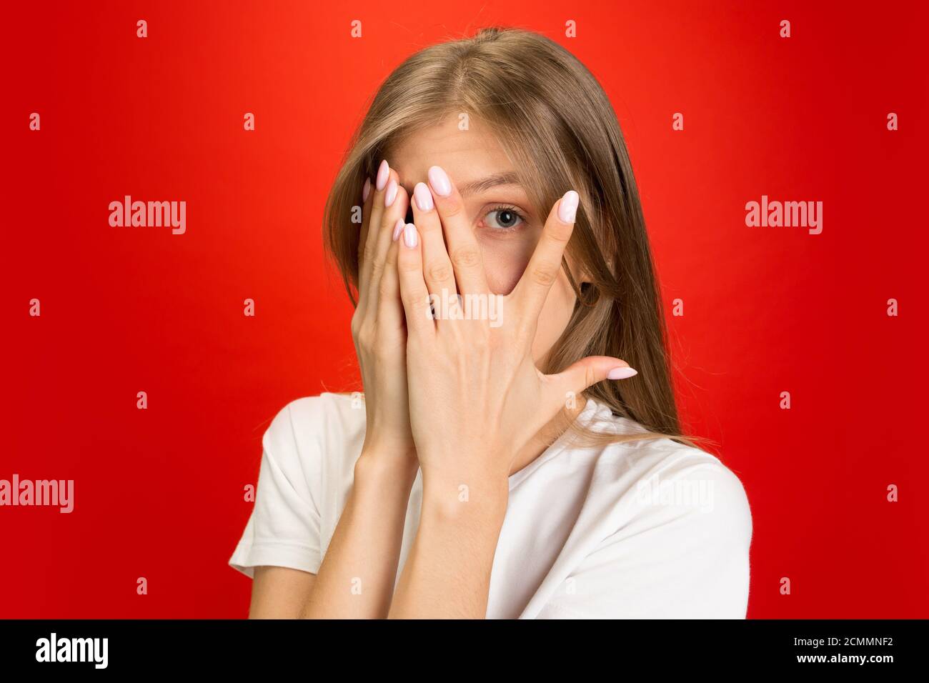 Scared hiding face. Portrait of young caucasian woman on red studio ...
