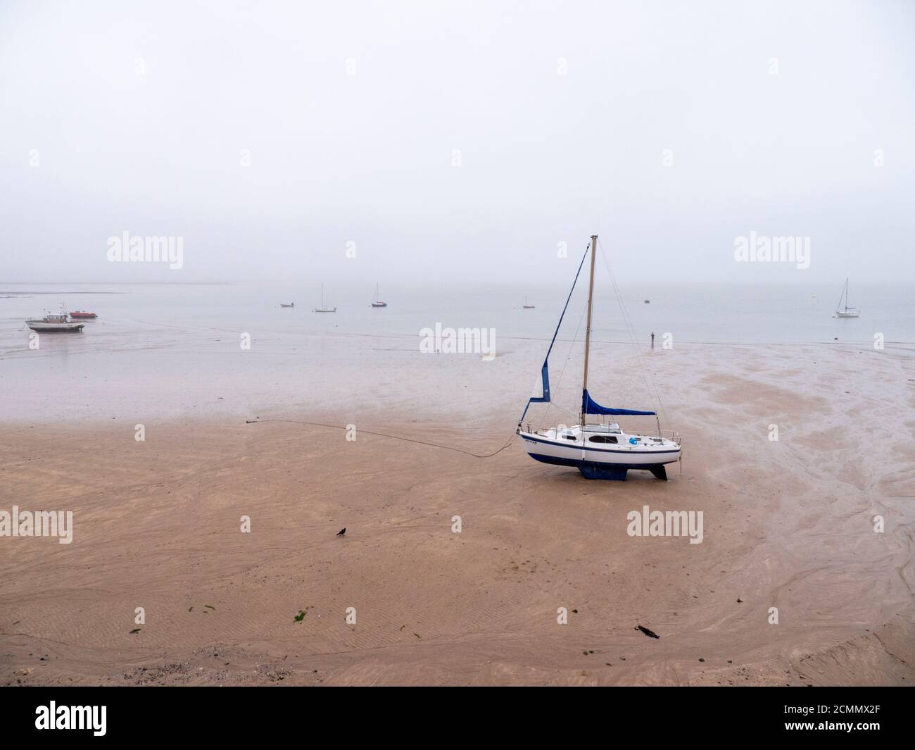 A fin keel yacht on the beach at low tide on a foggy day at the Mumbles ...