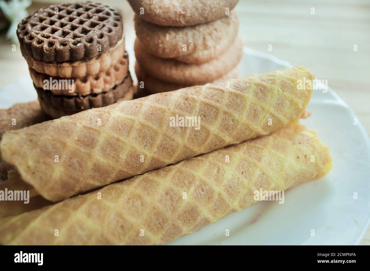 Waffle rolls and cookies on a white plate. Waffles in front ...