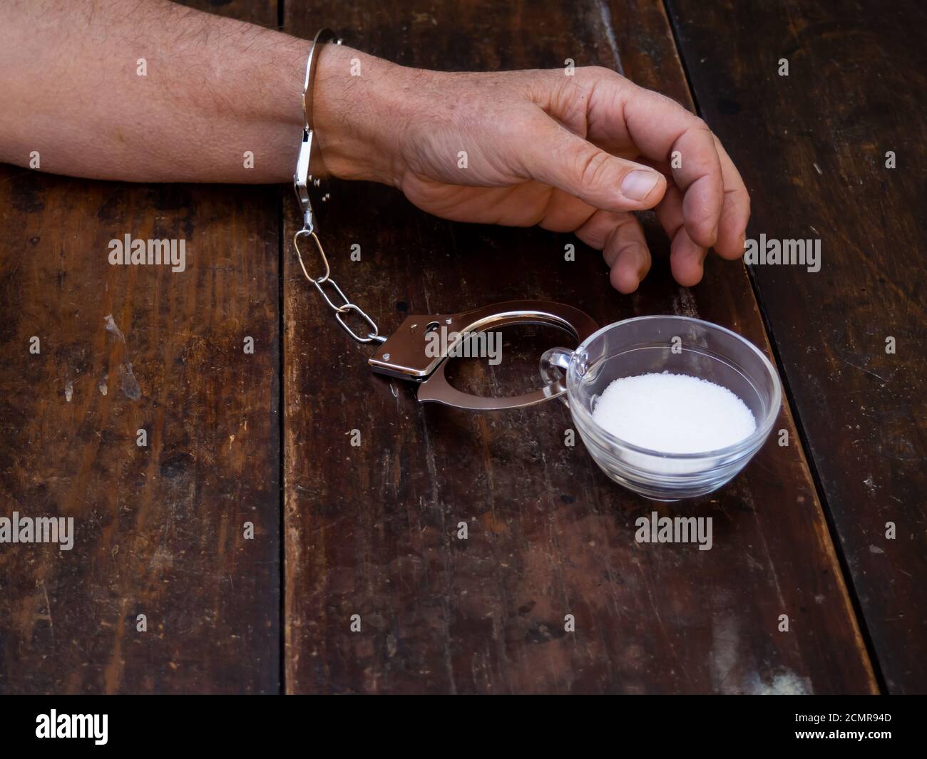 A man handcuffed to a cup with sugar. Food or sugar addiction concept ...
