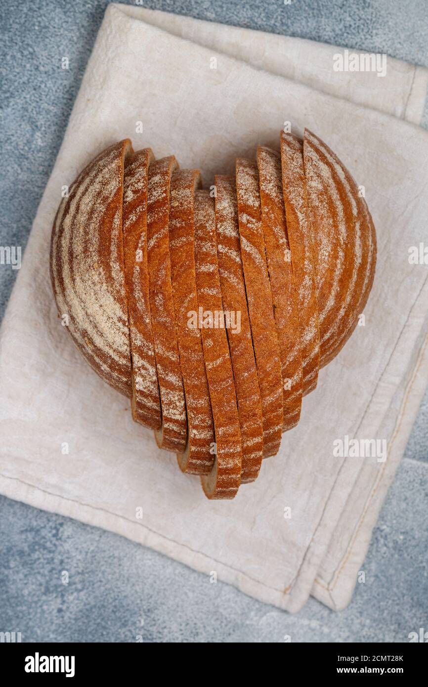 Sliced round loaf of rye bread in the shape of a heart on a gray linen ...