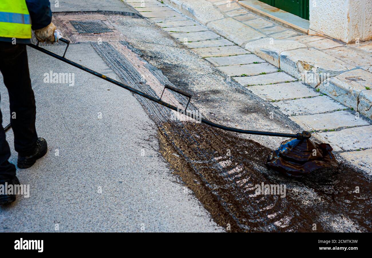Partial repair of the asphalt road. The worker sprays bitumen on the ...