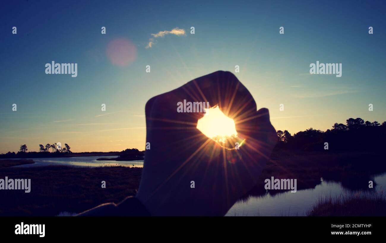 Hand in silhouette curled around sun to create sunburst Stock Photo - Alamy