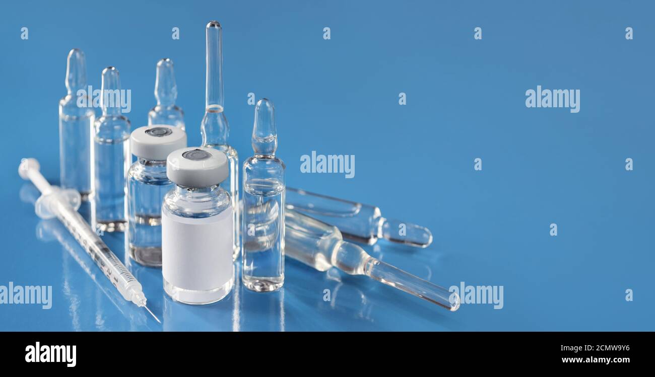 Vials of medicine, glass ampoules and a disposable syringe on a light ...