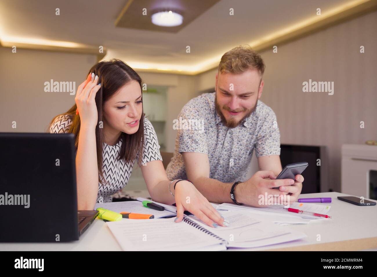 two students learning together, sitting at table in front of papers and ...