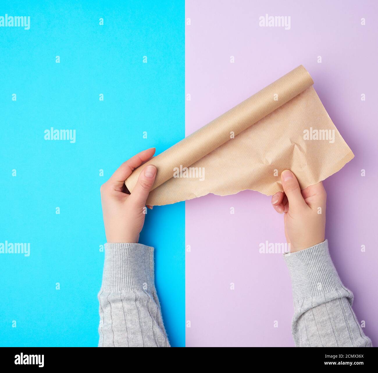 two hands holding a roll of brown parchment paper on a colored ...