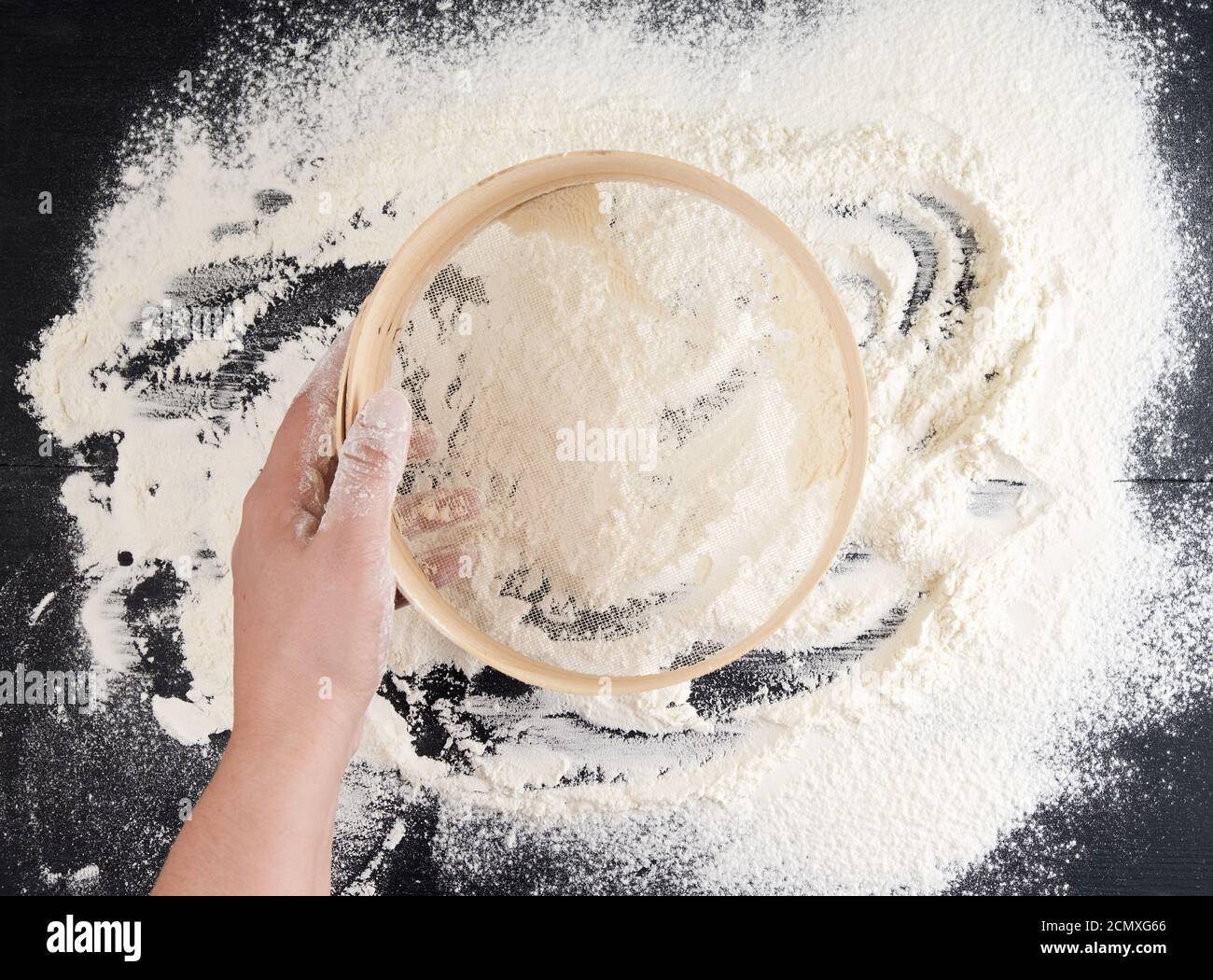 women's hands hold a round wooden sieve and sift white wheat flour ...