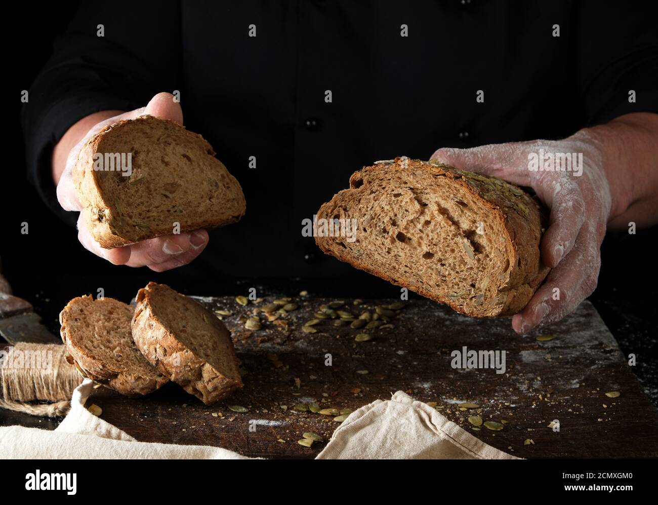 chef in black uniform keeps cut off a piece of bread baked from rye ...