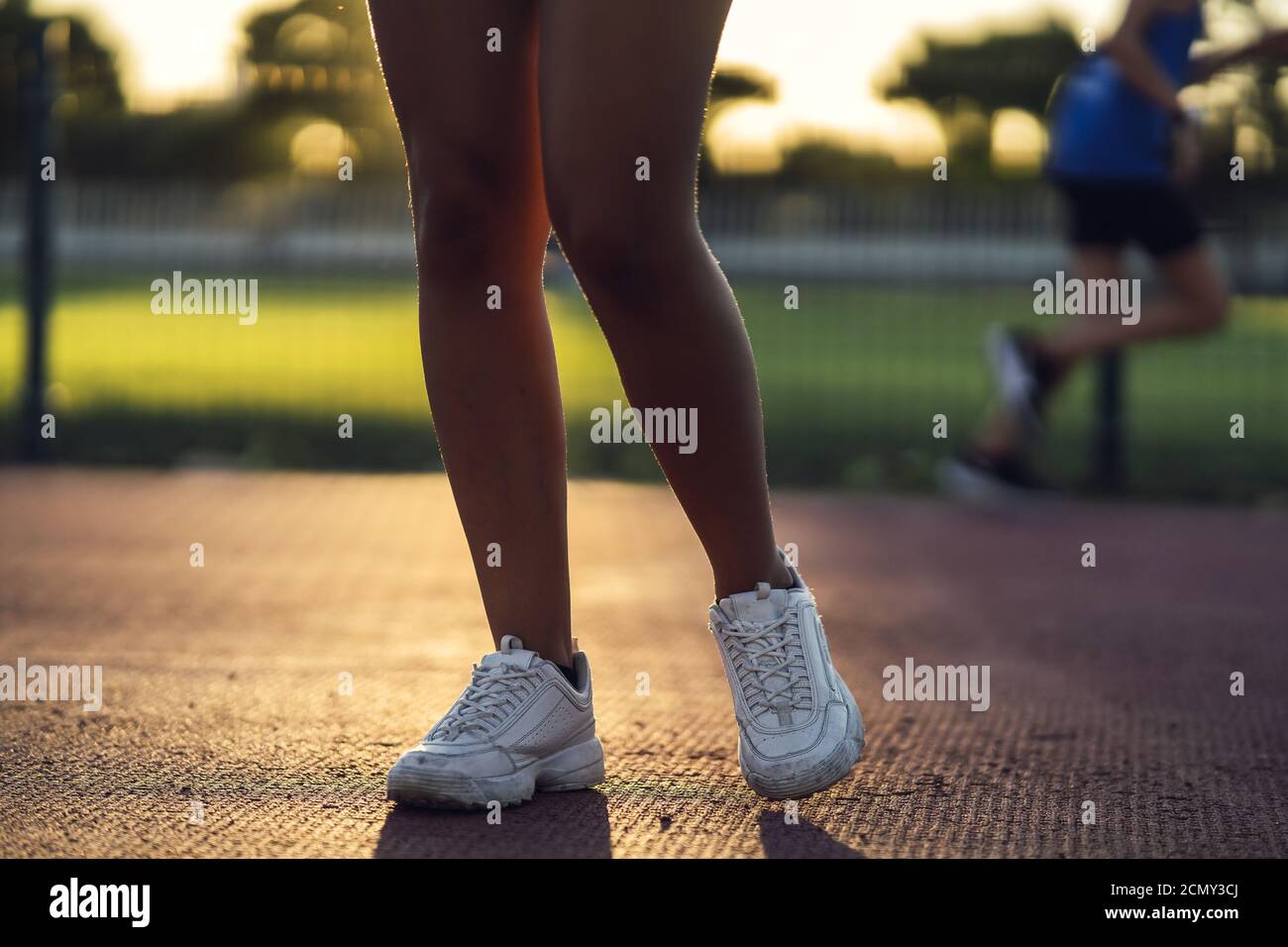 Closeup of a person in shorts and white trainers jogging in a park ...
