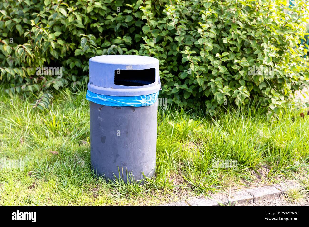 Closeup of a metallic garbage bin in a field covered in greenery under ...